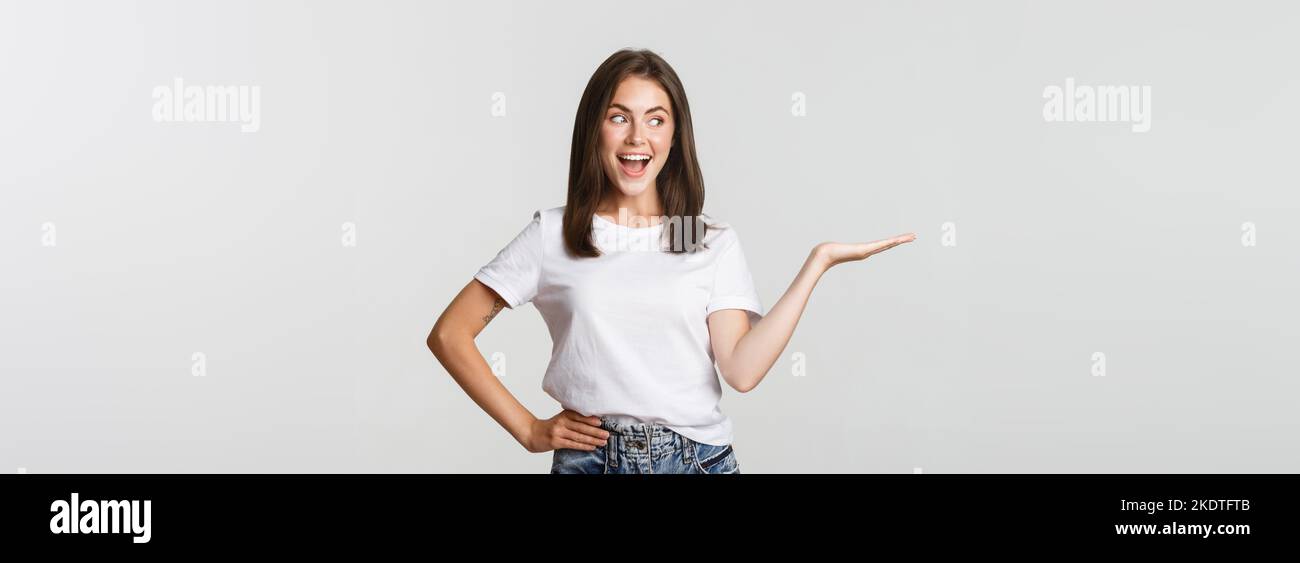 Excited beautiful girl extend arm, holding something on hand and ...