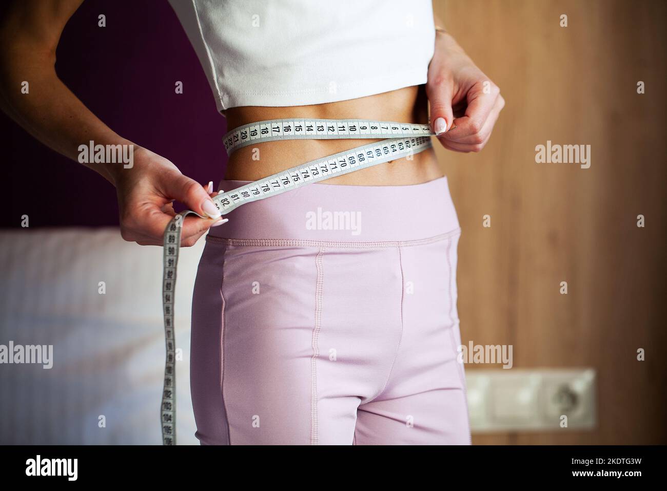 Slim young woman measuring her thin waist with a tape measure at home ...