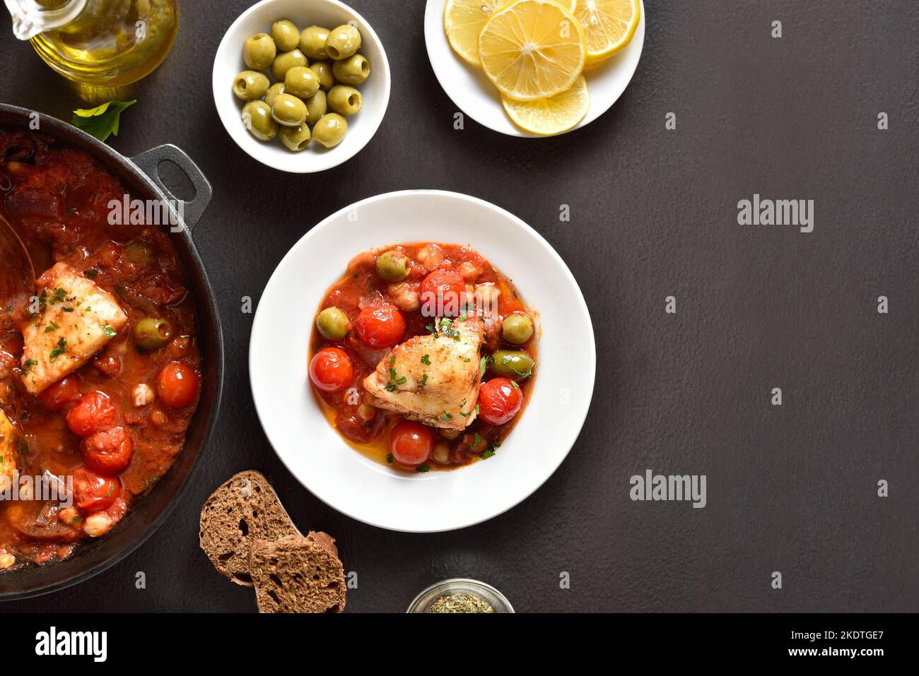 Cod stew with chickpeas, cherry tomatoes and olives on plate over dark background with copy ...