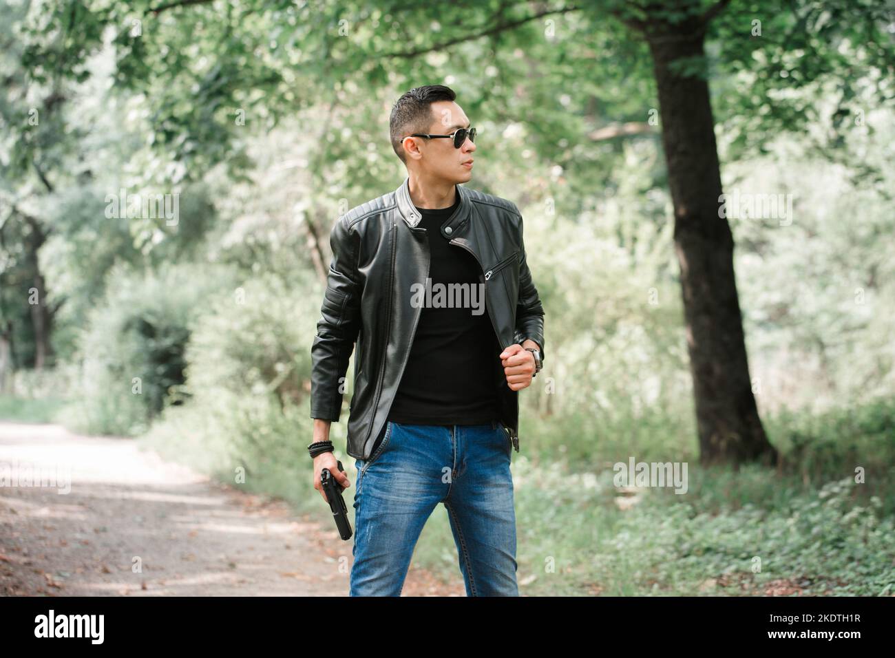 A man in dark glasses and a black leather jacket holds a gun in his ...