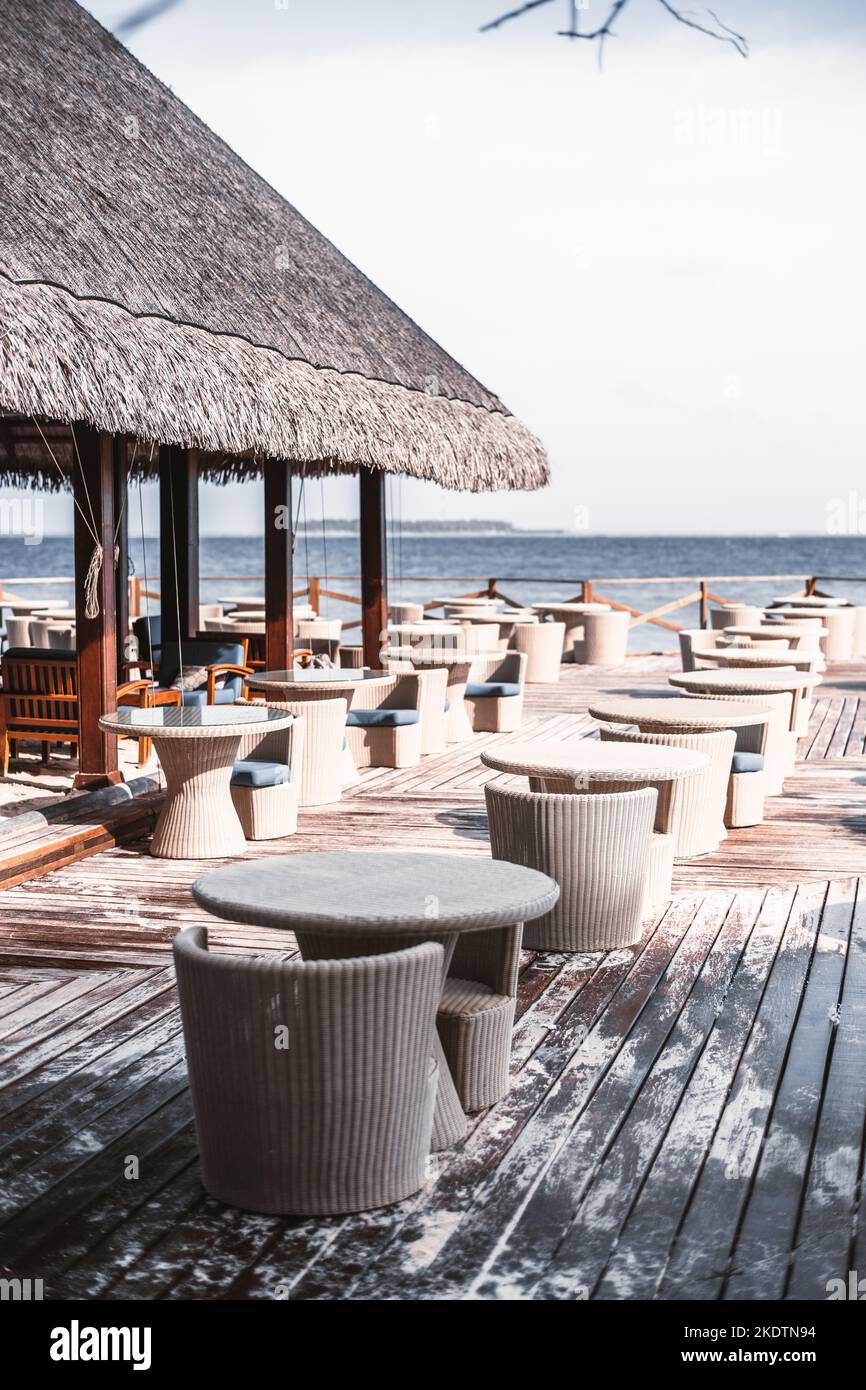 A vertical shot of a row of empty wicker cafe tables with chairs of an ...