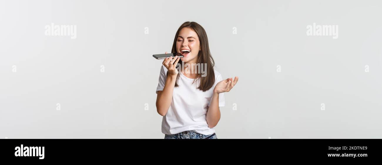 Friendly attractive brunette girl talking on speaker, record voice ...