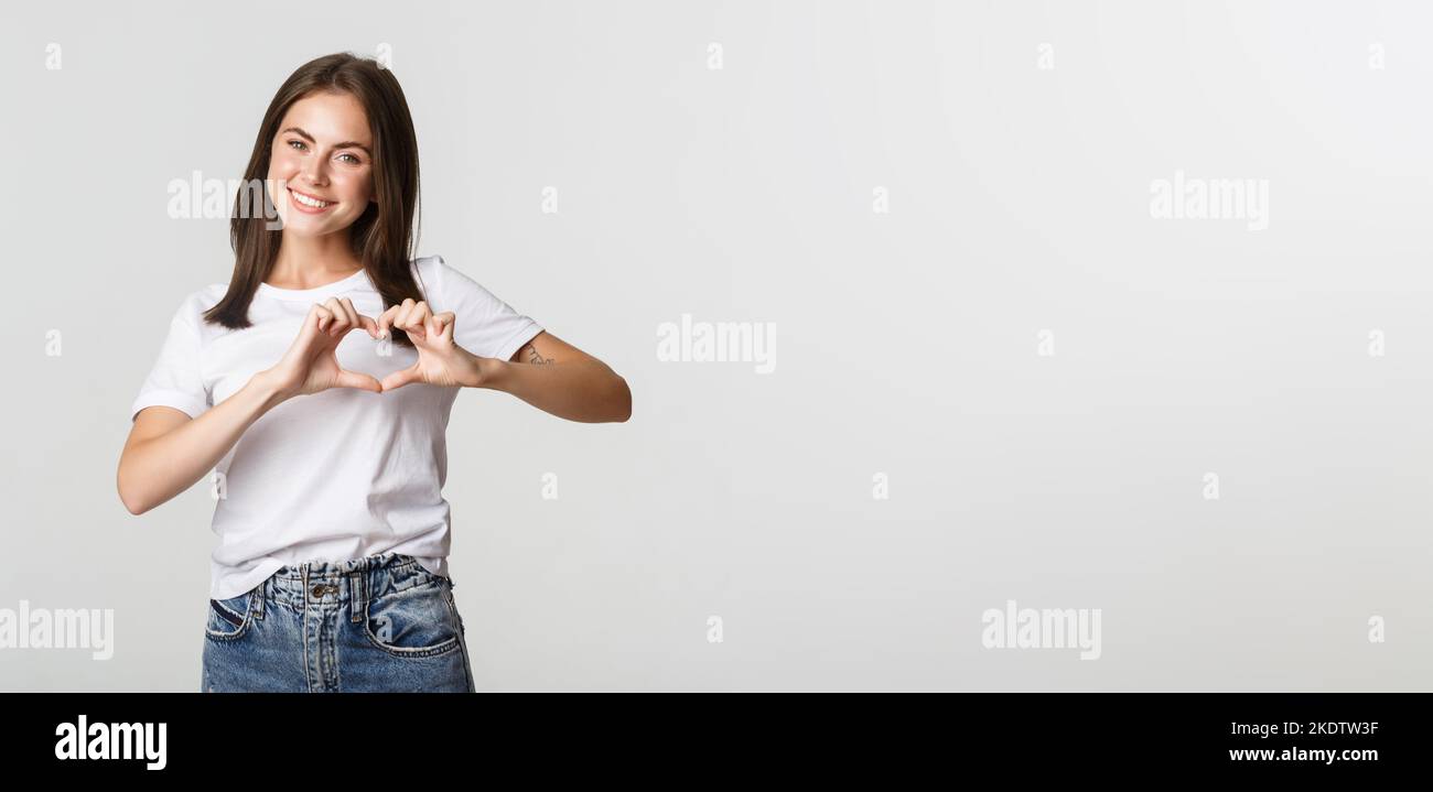 Tender beautiful brunette girl showing heart gesture, express love and ...