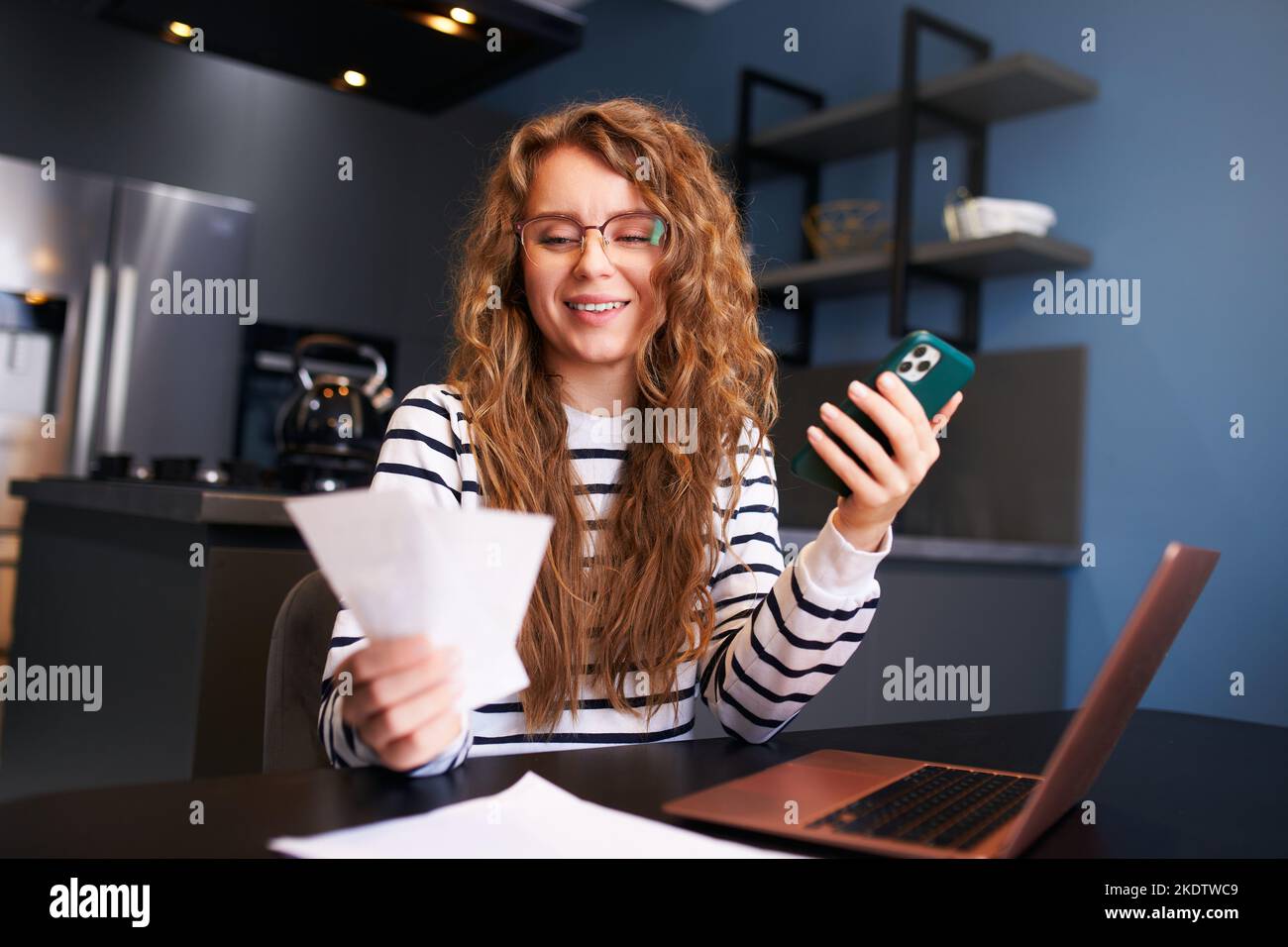 Happy woman using online banking app to pay bills, holding paychecks ... Happy woman using online banking app to pay bills, holding paychecks ...
