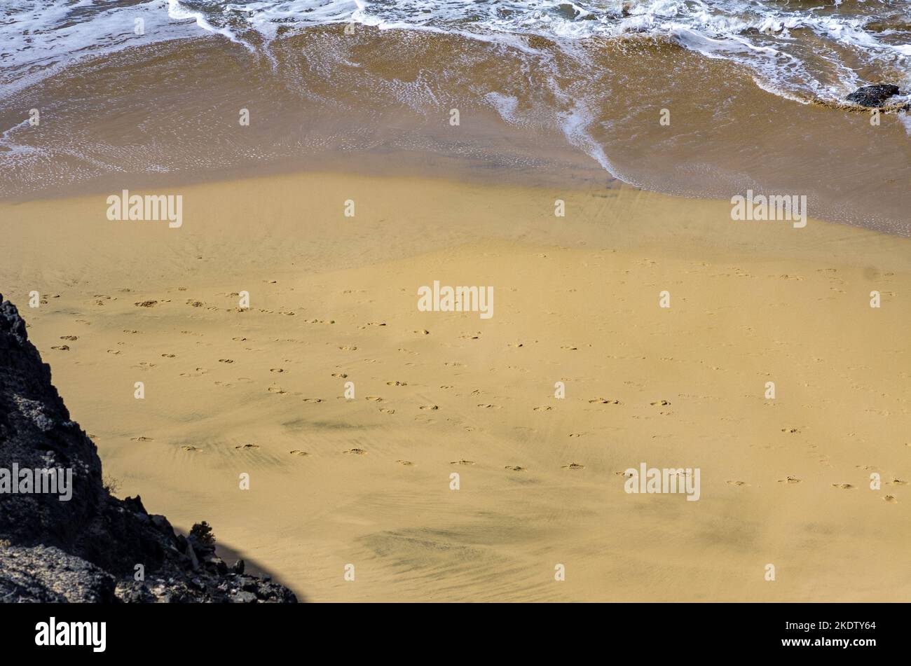Footprints on golden beach, foaming sea at top of image, photographed ...