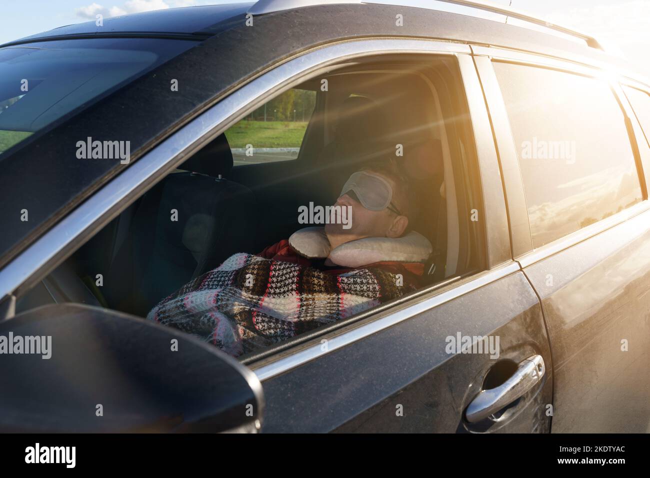 A tired driver sleeps in the car during the day, covered with a blanket ...
