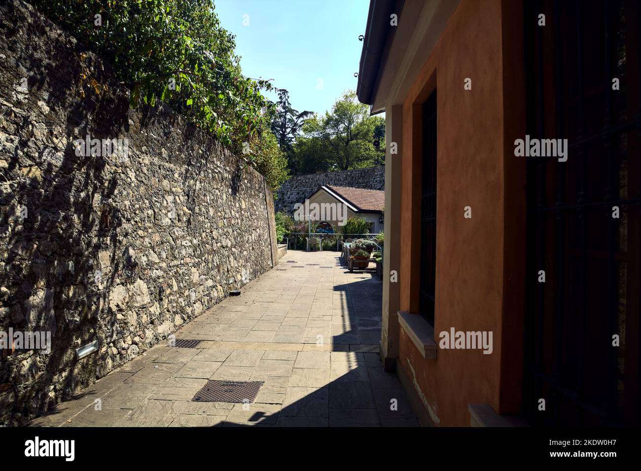 Paved path in a park between a stone wall and a building on a sunny day ...