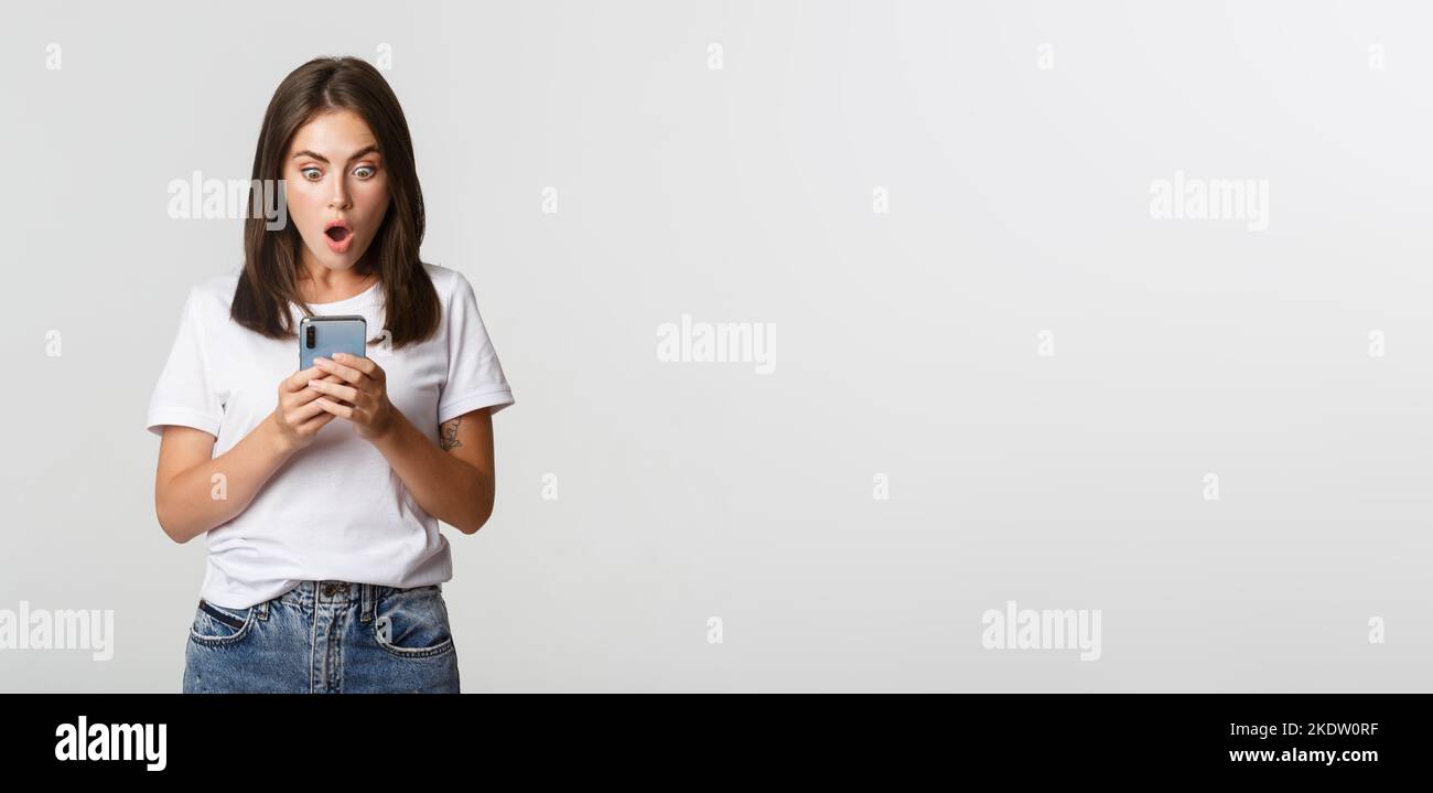 Shocked and impressed brunette girl looking amazed at smartphone screen ...