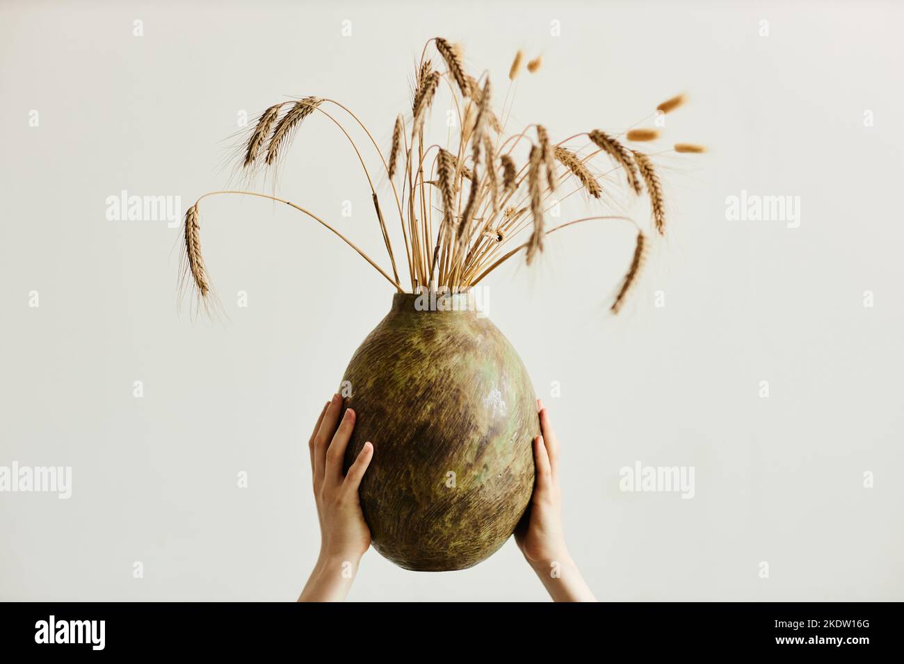Minimal closeup of hands holding handmade ceramic vase with wheat ...