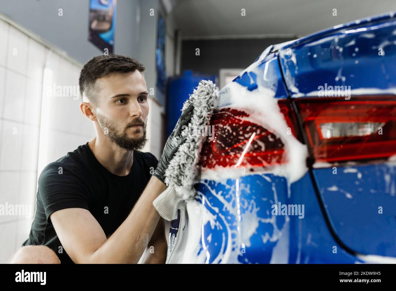 Hand washing with microfiber glove with foam car body in garage. Car ...