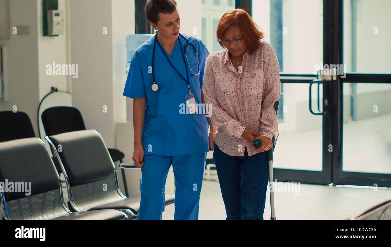 Asian woman with impairment walking with cane, nurse giving support and ...