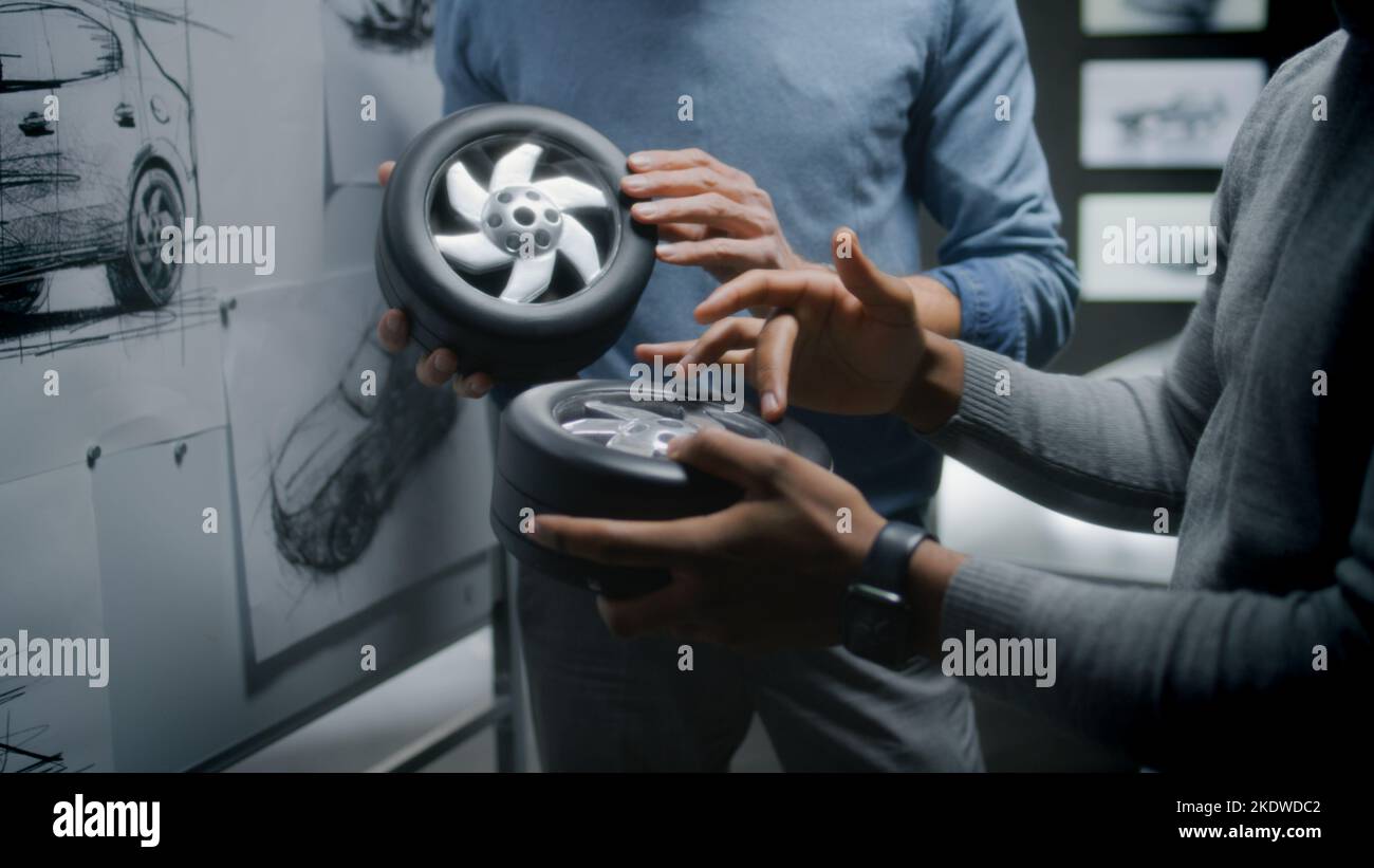 Two diverse automotive male designers holding small wheels, developing futuristic electric car ...