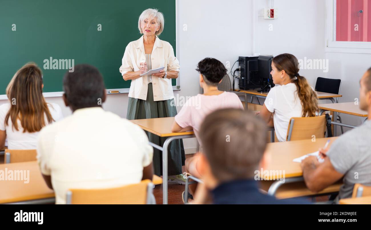 Elderly female teacher giving lecture to group of students in ...