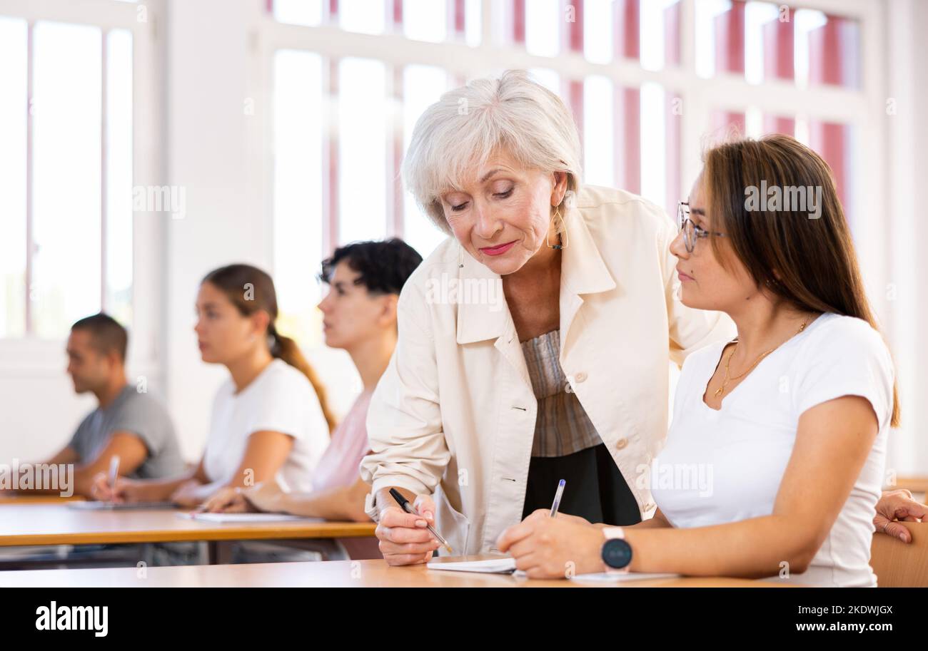 Elderly female teacher helping to solve problem to young girl student ...