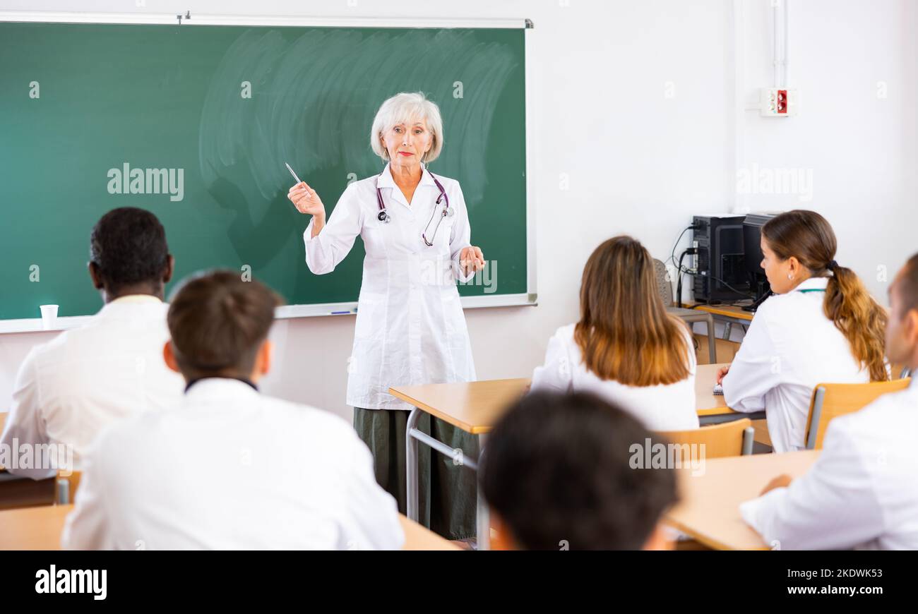 Elderly female professor of medicine giving lecture to students at ...