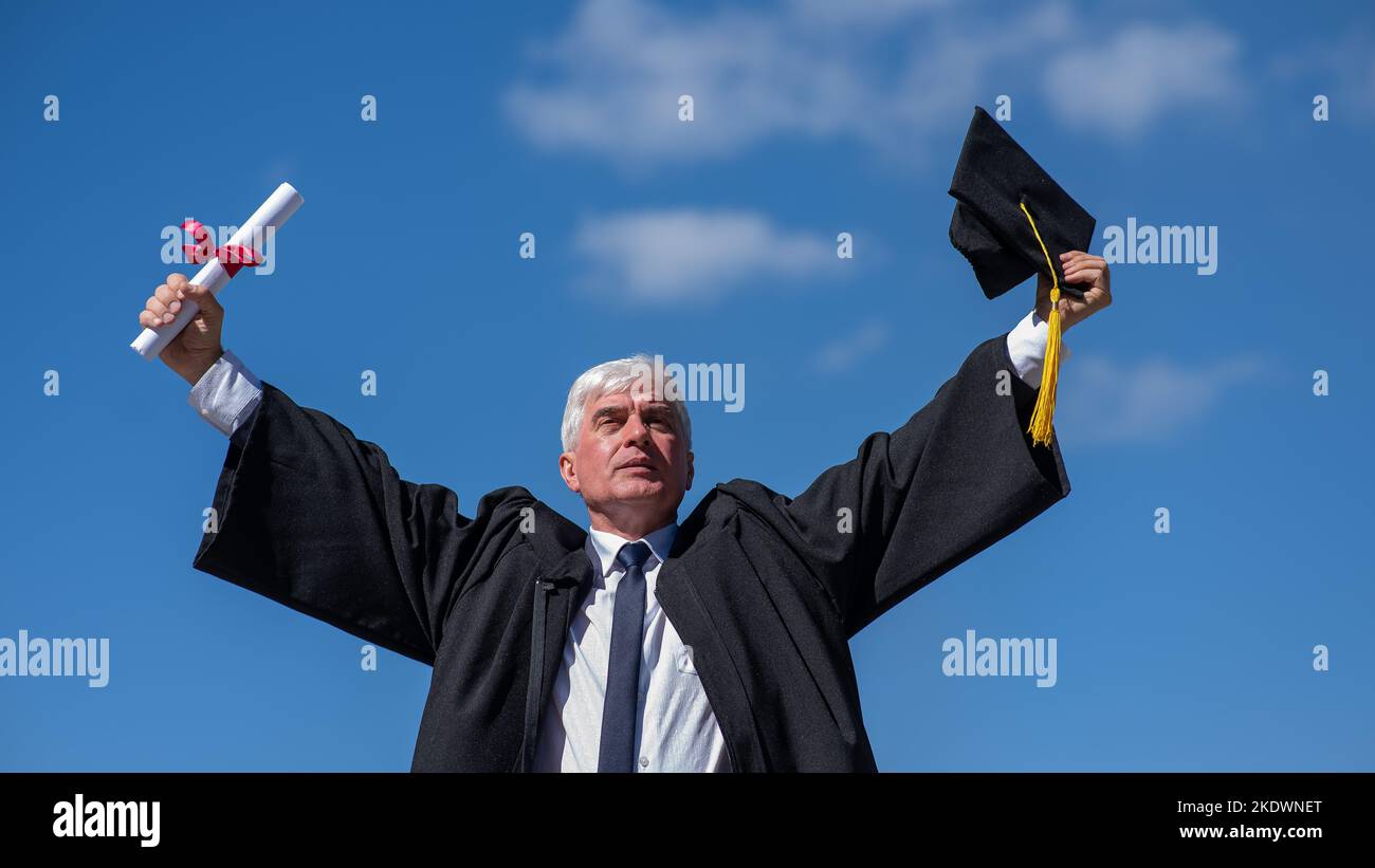 Elderly male graduate rejoices in receiving a diploma against a blue ...
