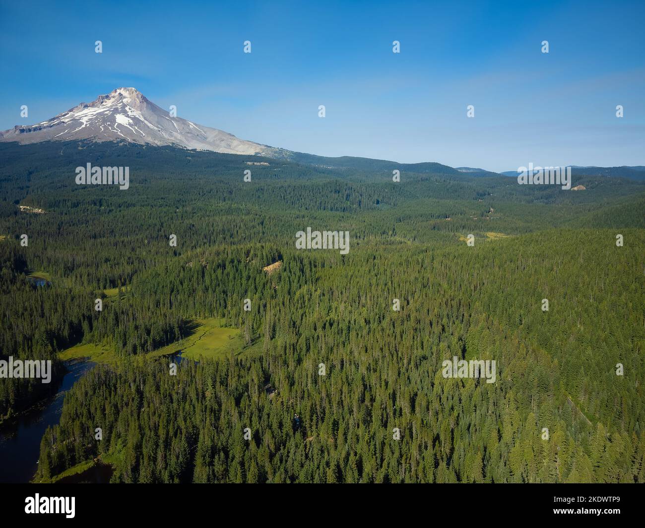 A hilly area covered with green grass, a small stream and a high snow ...