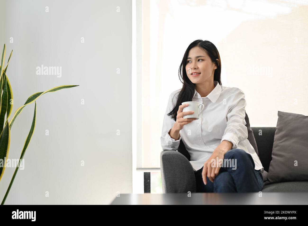 Attractive young Asian woman relaxes sipping morning coffee while ...