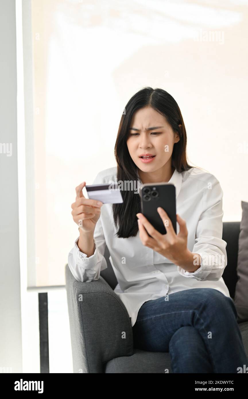 Unhappy and dissatisfied Asian woman sitting on sofa, looking at her ...
