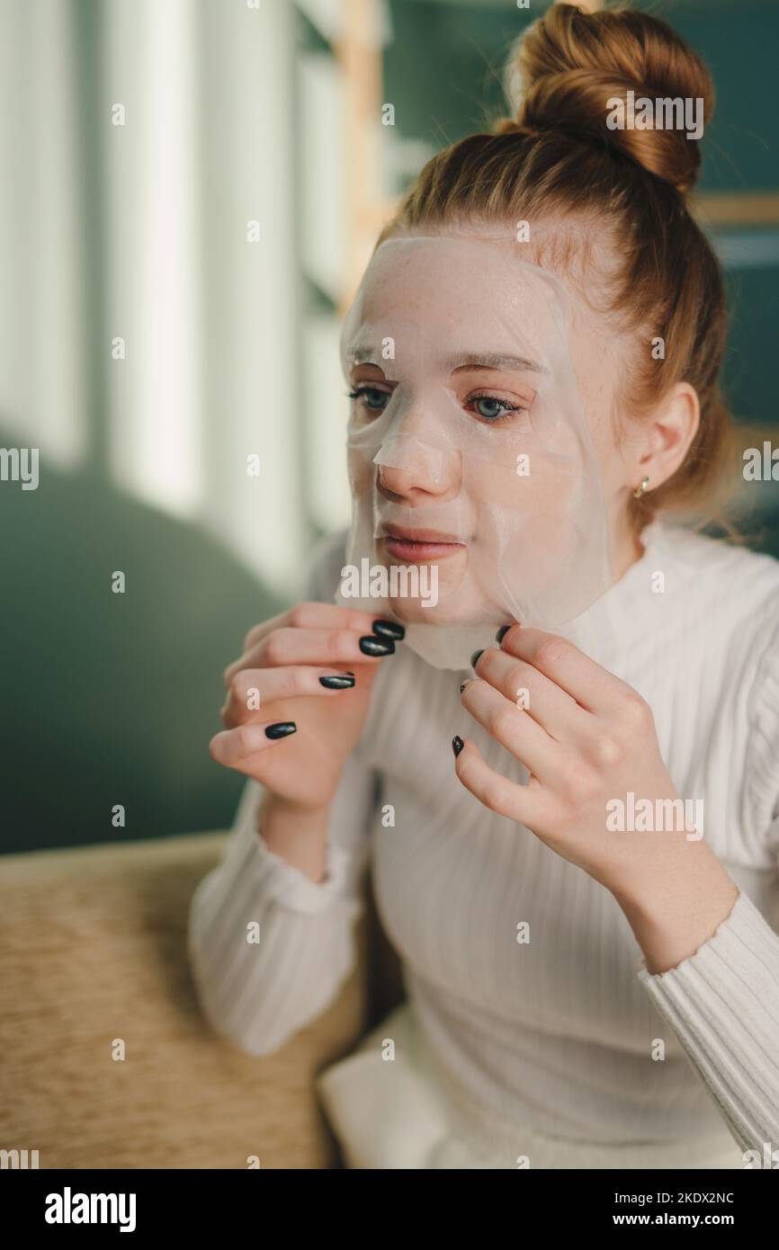 Young woman sitting on the sofa in the living room apply facial paper ...