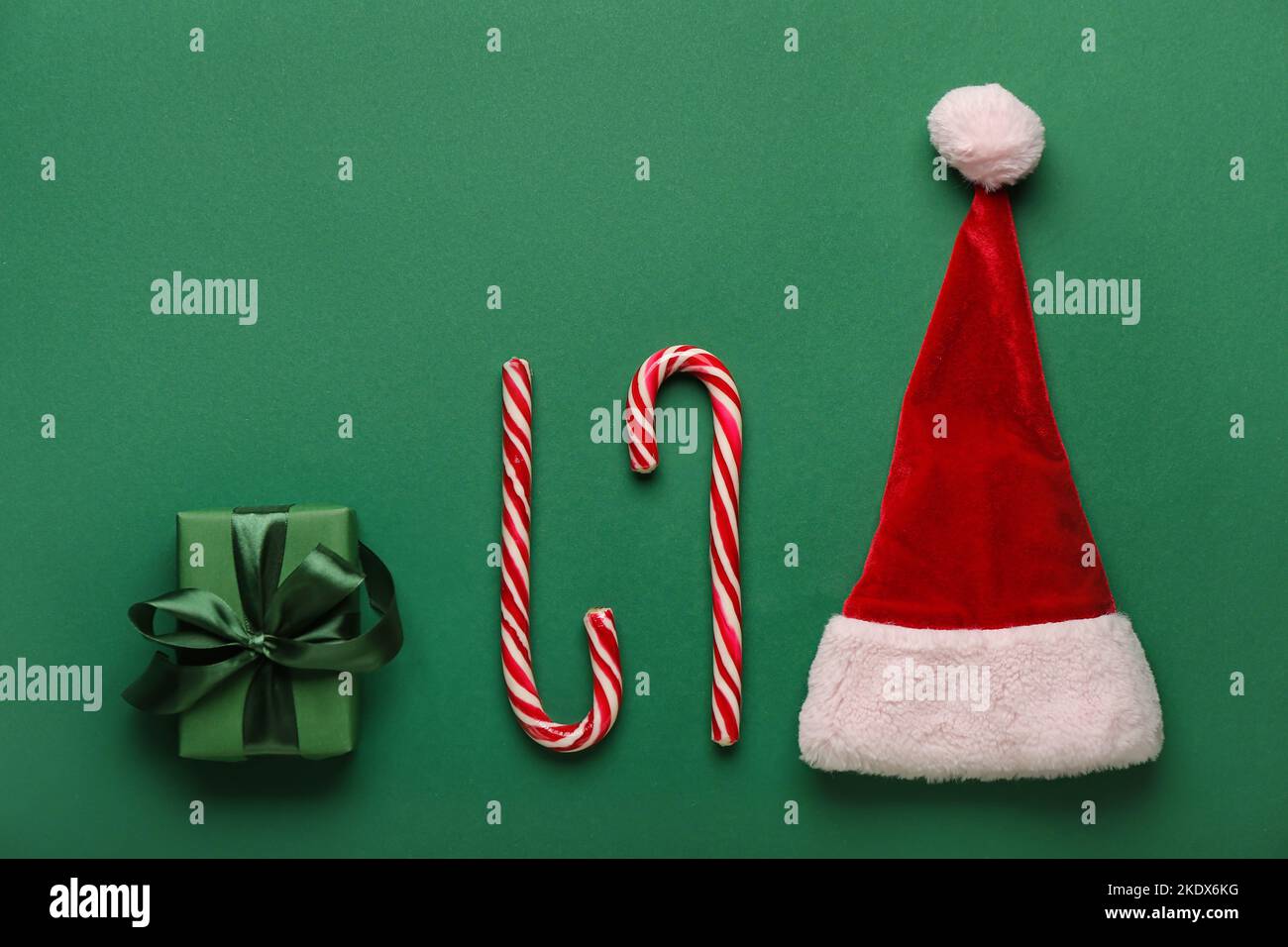 Candy canes with Christmas gift and Santa hat on green background Stock ...