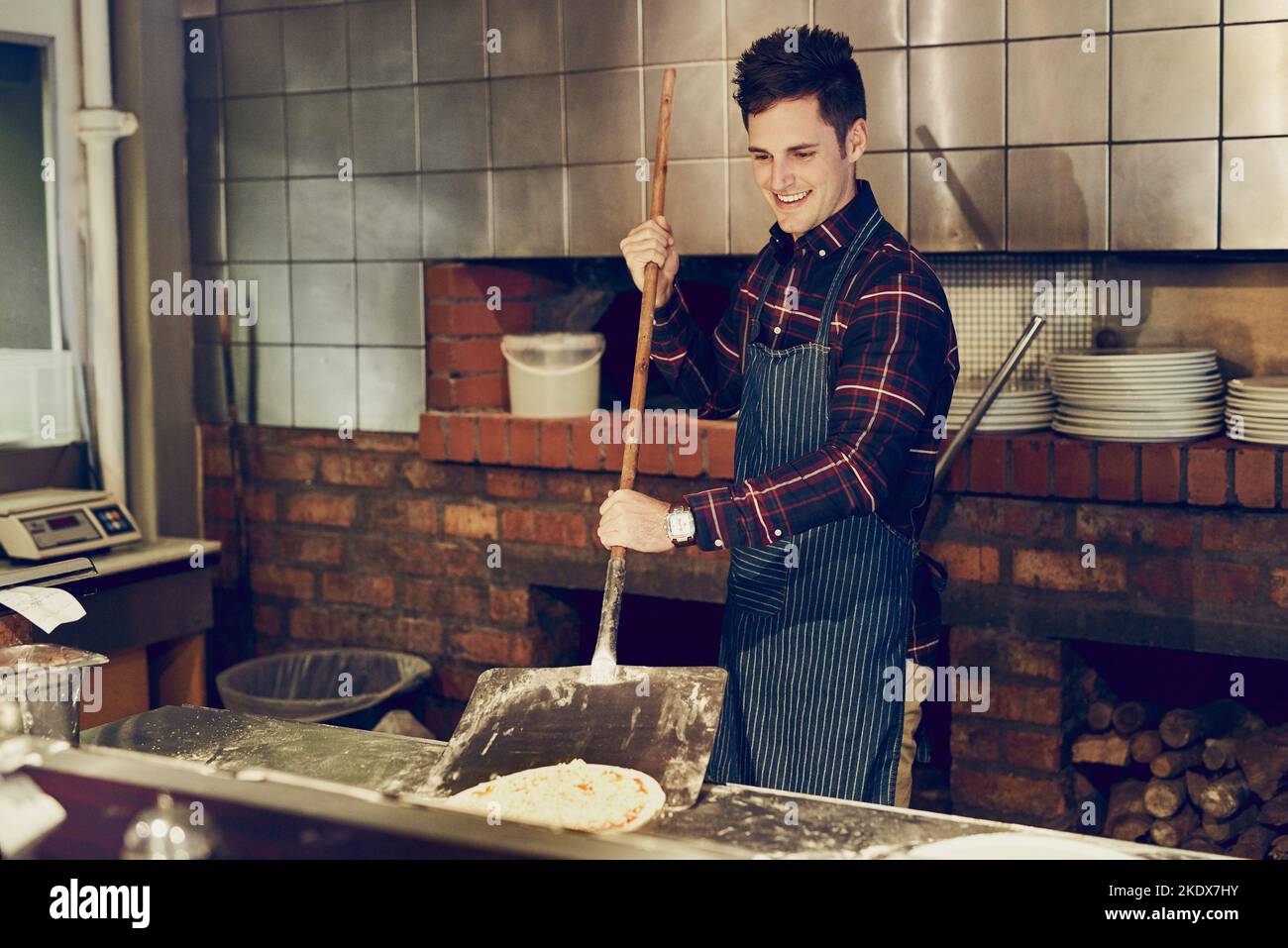 He makes pizza to perfection. a young man using a peel while making a ...