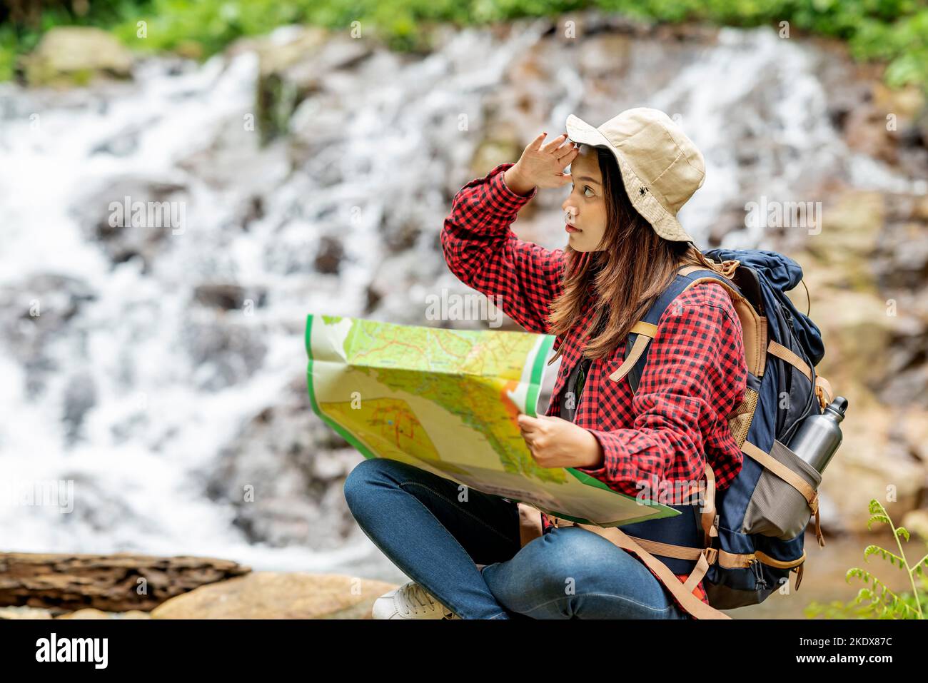 Asian woman in a hat and backpack holding maps looking around with a ...