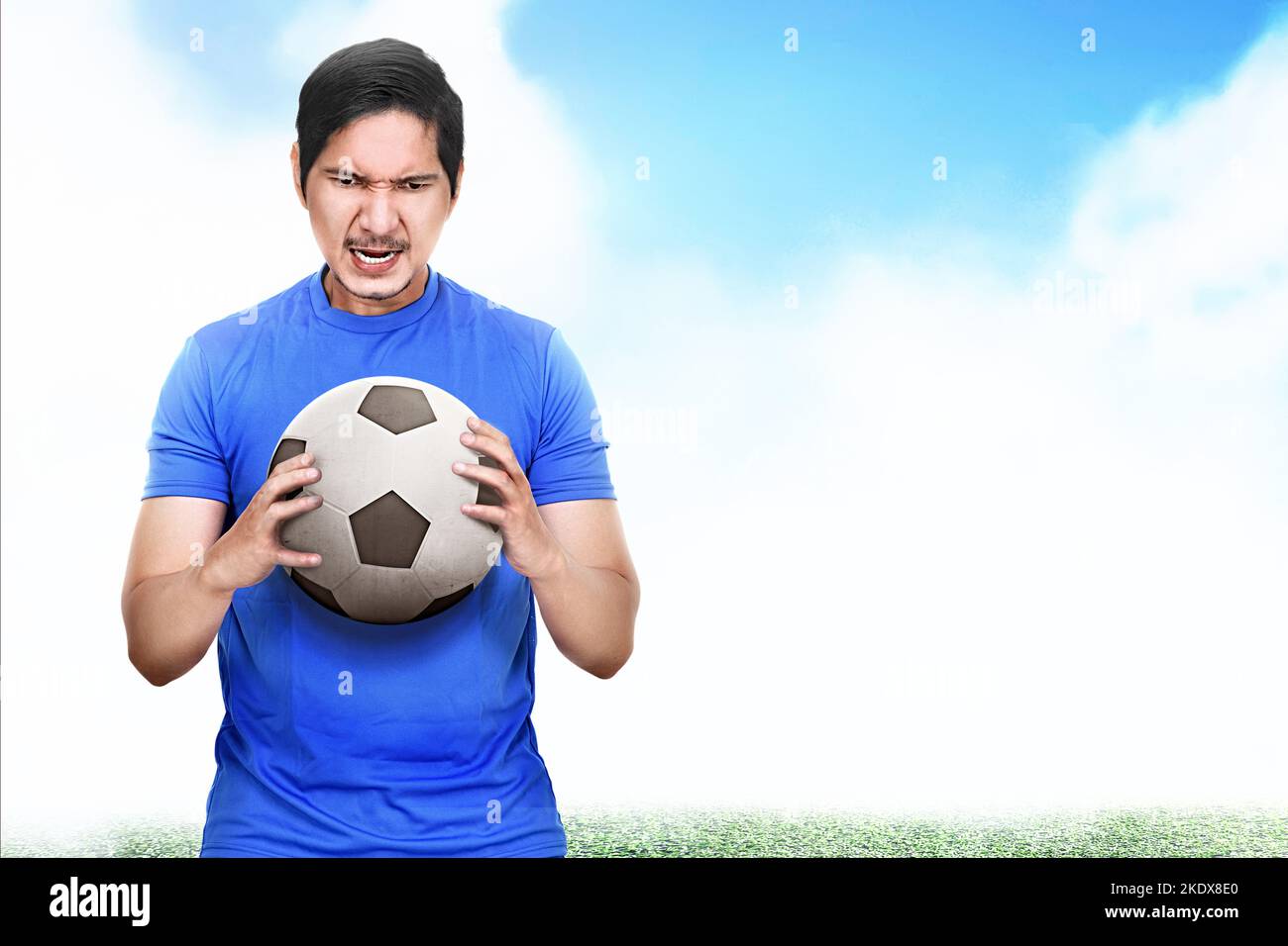 An Asian football player man in a blue jersey is standing and holding ...