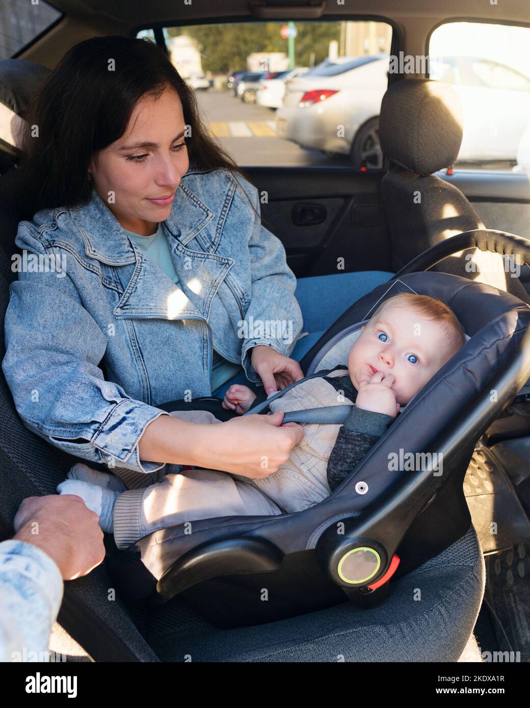 Mother fastening baby to child safety seat inside of car. Kid baby boy ...