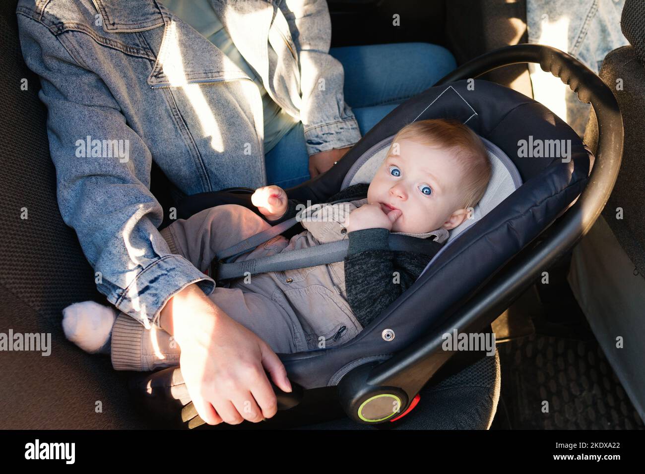 Mother fastening baby to child safety seat inside of car. Kid baby boy ...