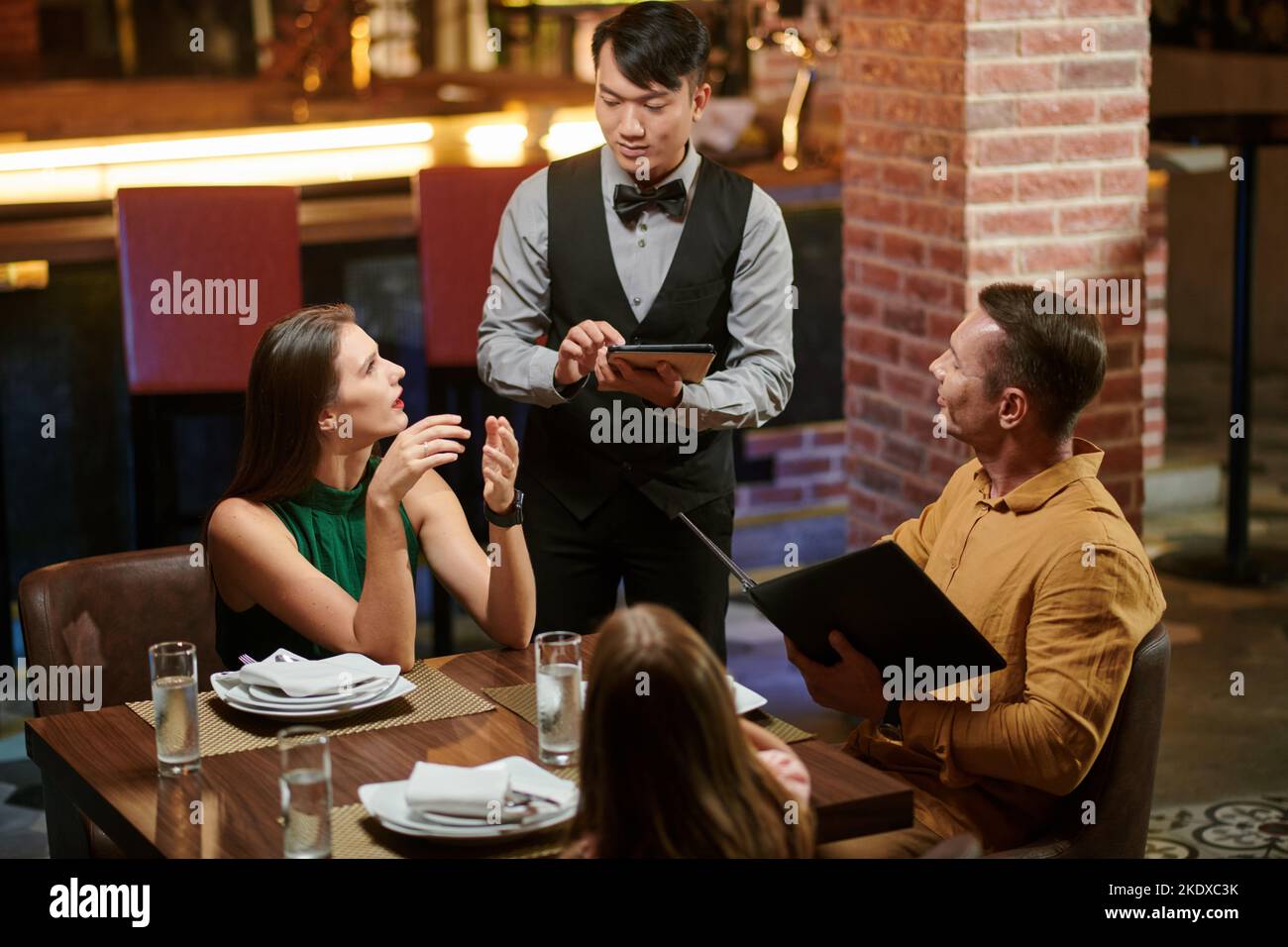Woman asking waiter to recommend her dish when eating in restaurant ...