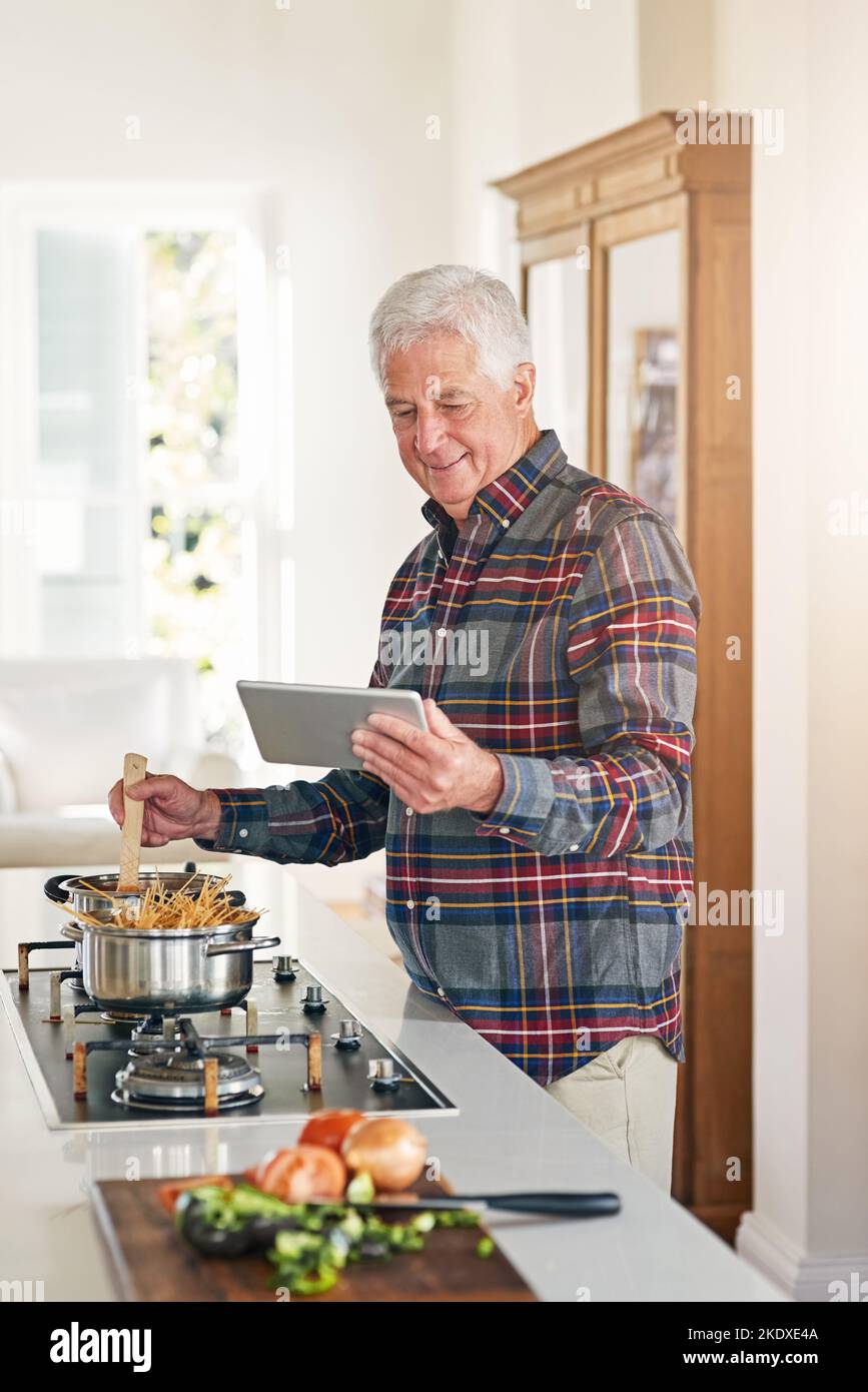 The kitchen is his kingdom. a senior man using a digital tablet while ...