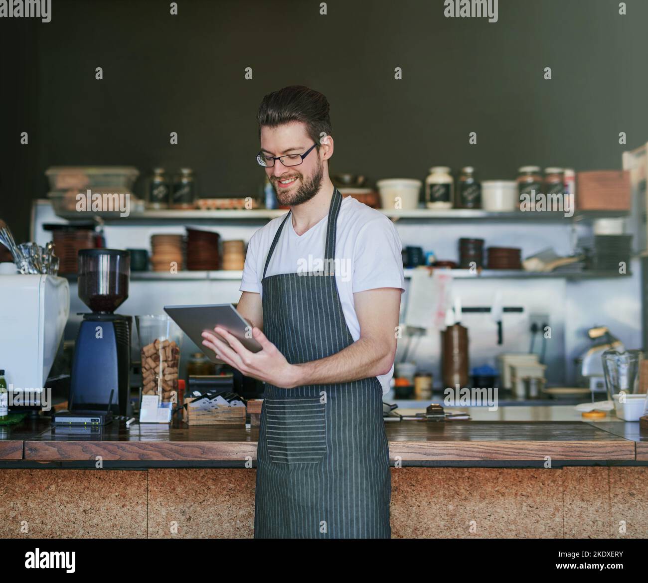 Managing his coffee shop online. a young barista using a tablet in his ...