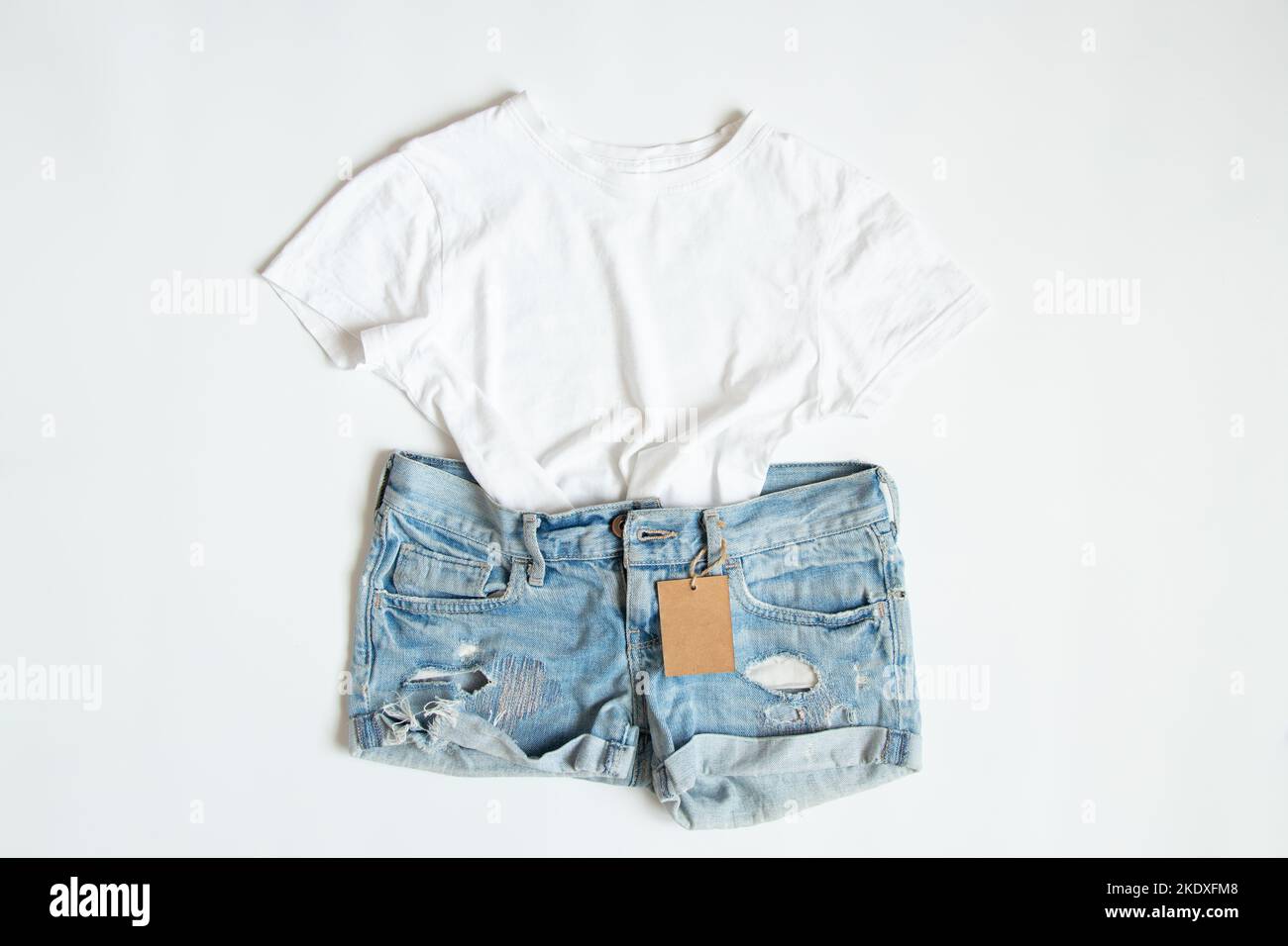 White t-shirt and denim shorts lie on a white background with a price tag, clothing sale ...