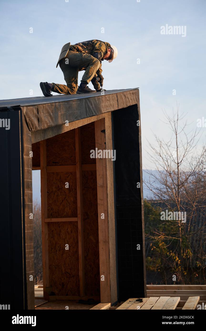 Male builder installing black corrugated iron sheet used as facade of ...