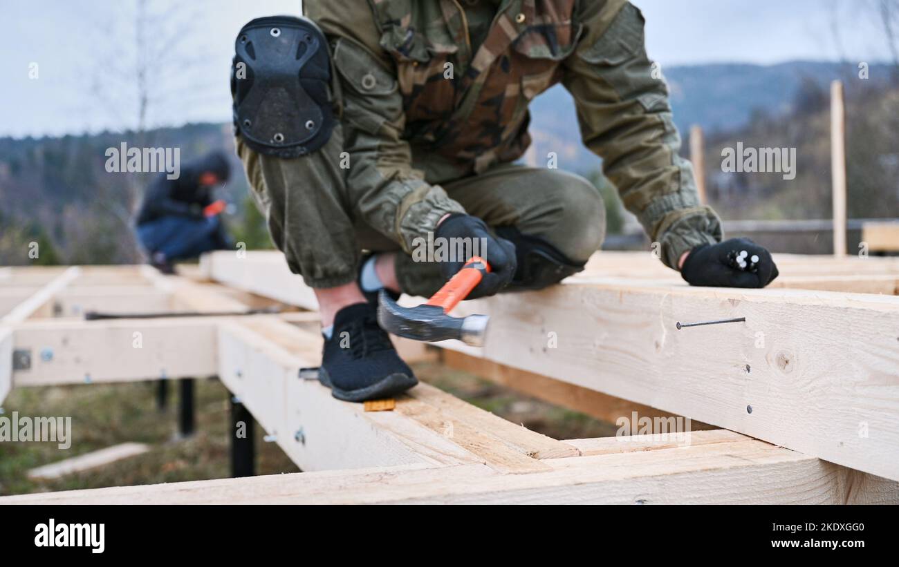 Man worker building wooden frame house. Carpenter hammering nail into ...
