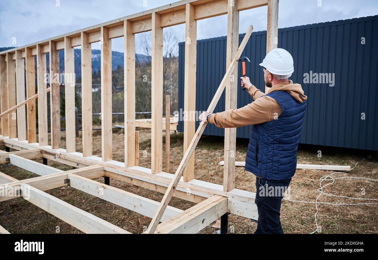 Man worker building wooden frame house on pile foundation. Carpenter ...