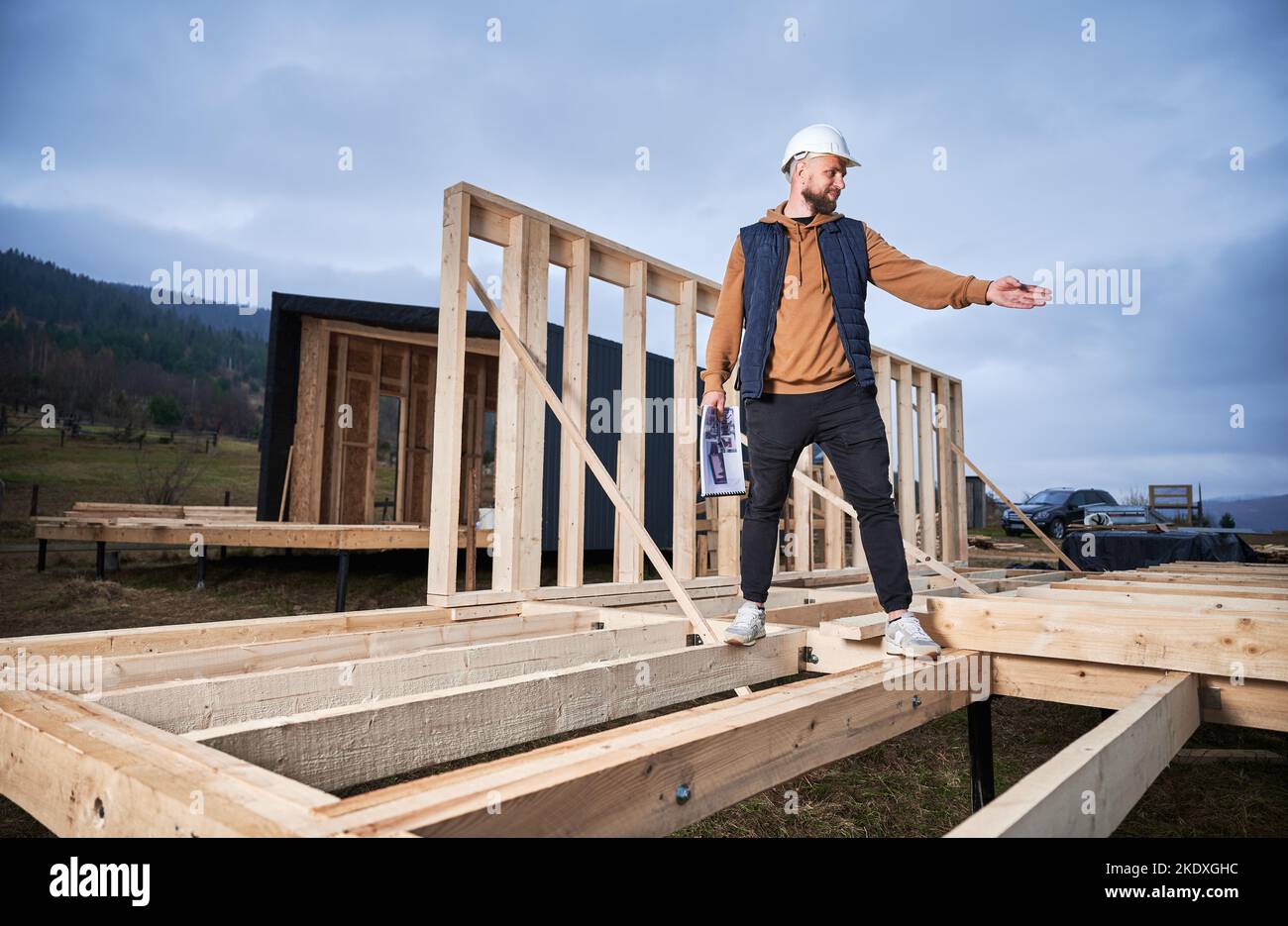 Male engineer building wooden frame house. Man builder standing on construction site in safety ...