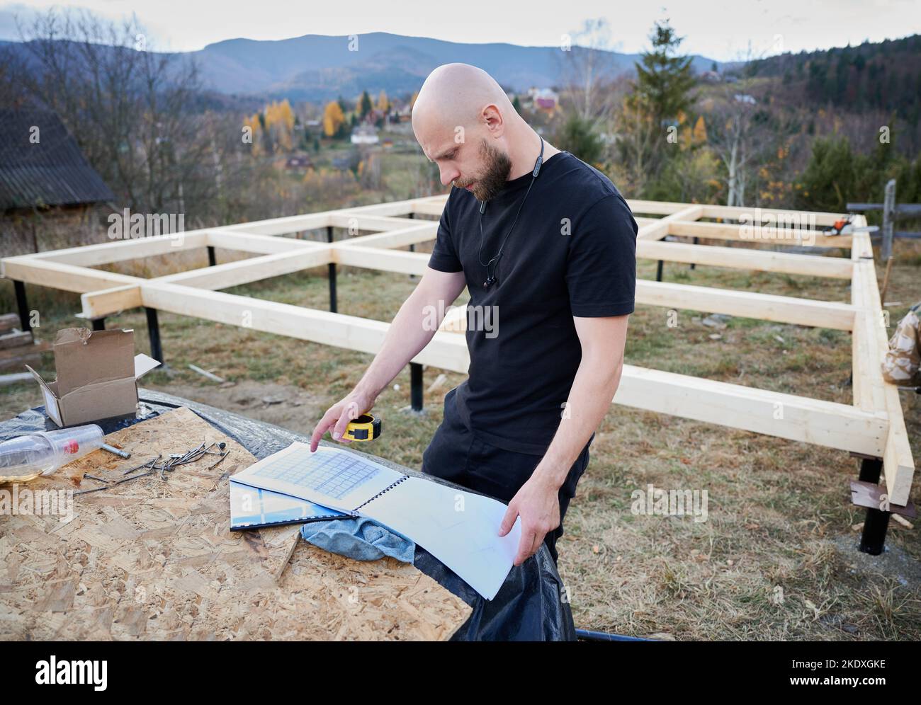 Male engineer building wooden frame house on pile foundation. Man builder standing on ...
