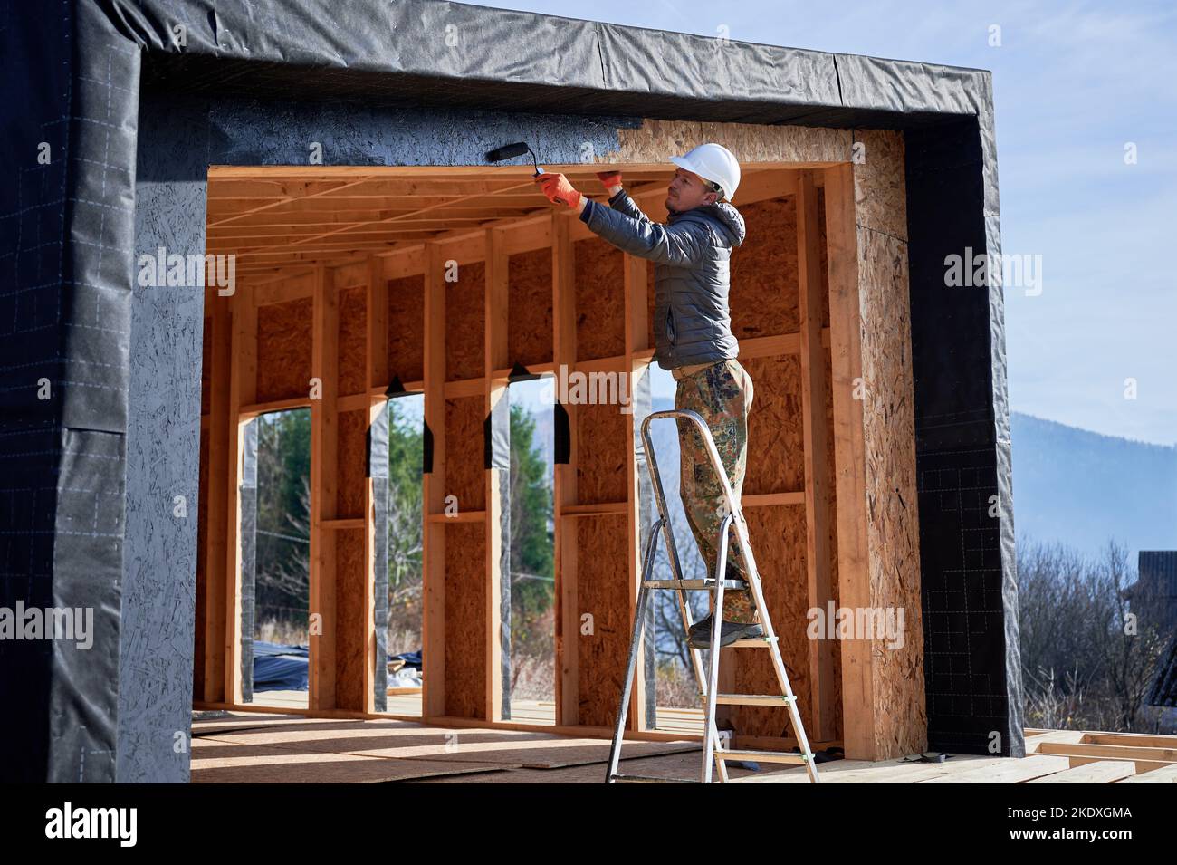 Male painter using paint roller, doing exterior paint work in a black ...