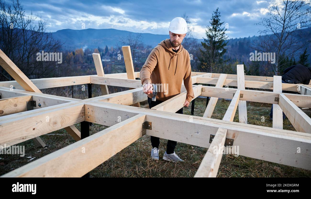 Men workers building wooden frame house on pile foundation. Carpenters installing wooden joist ...