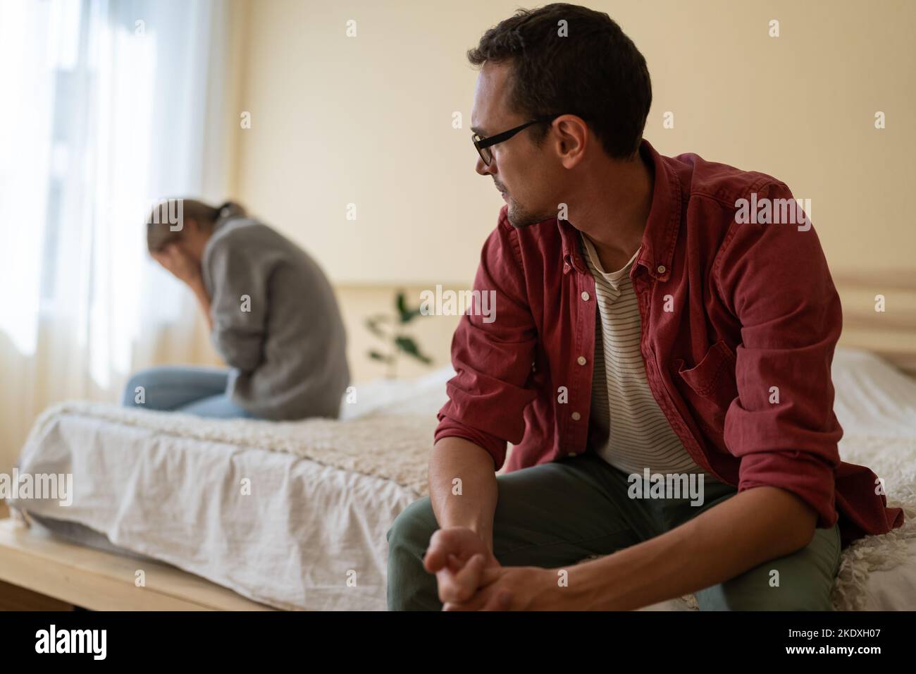 Confused man looks towards crying girl sits on opposite side of bed ...