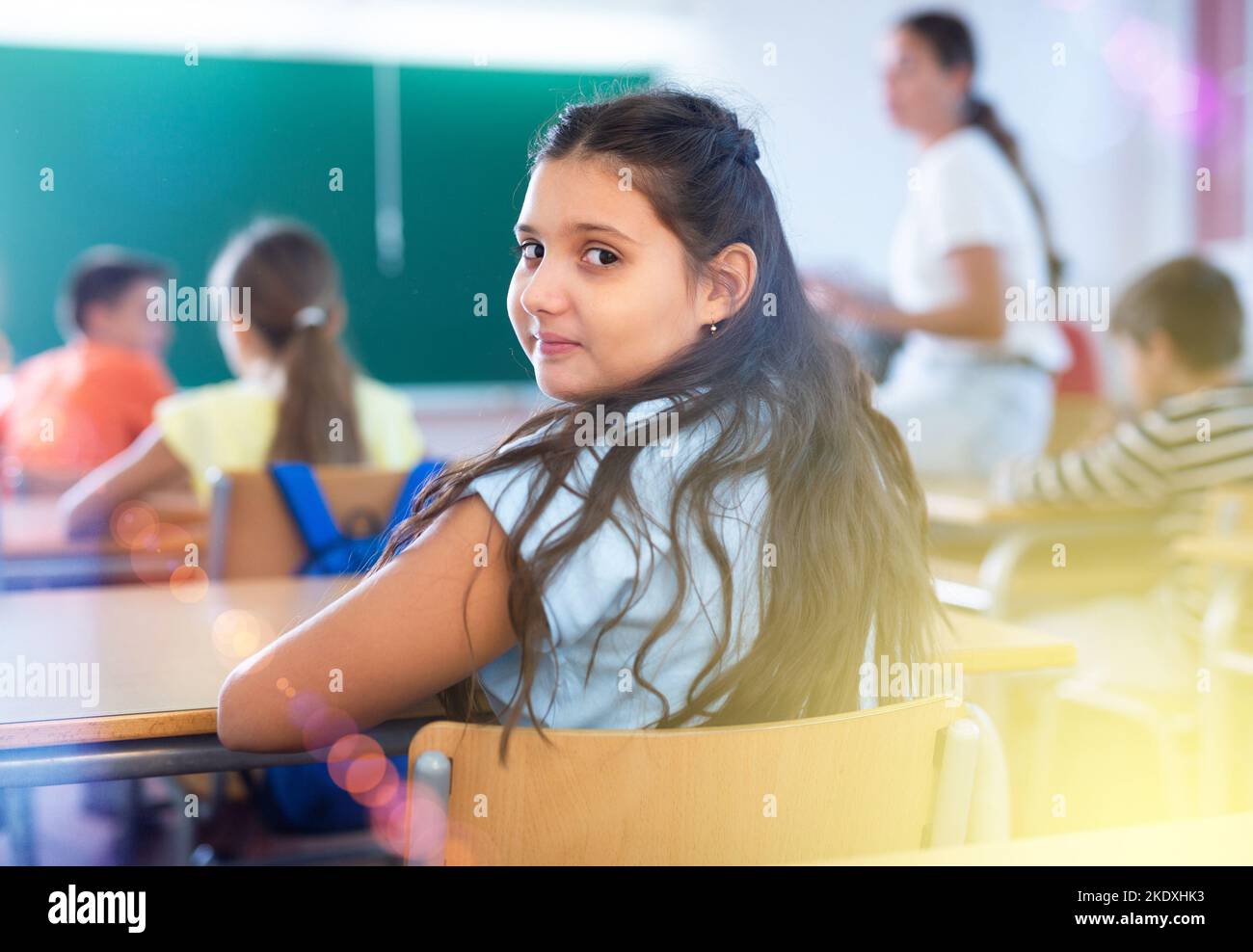 Schoolgirl sits half-turned at desk in classroom at lesson in ...