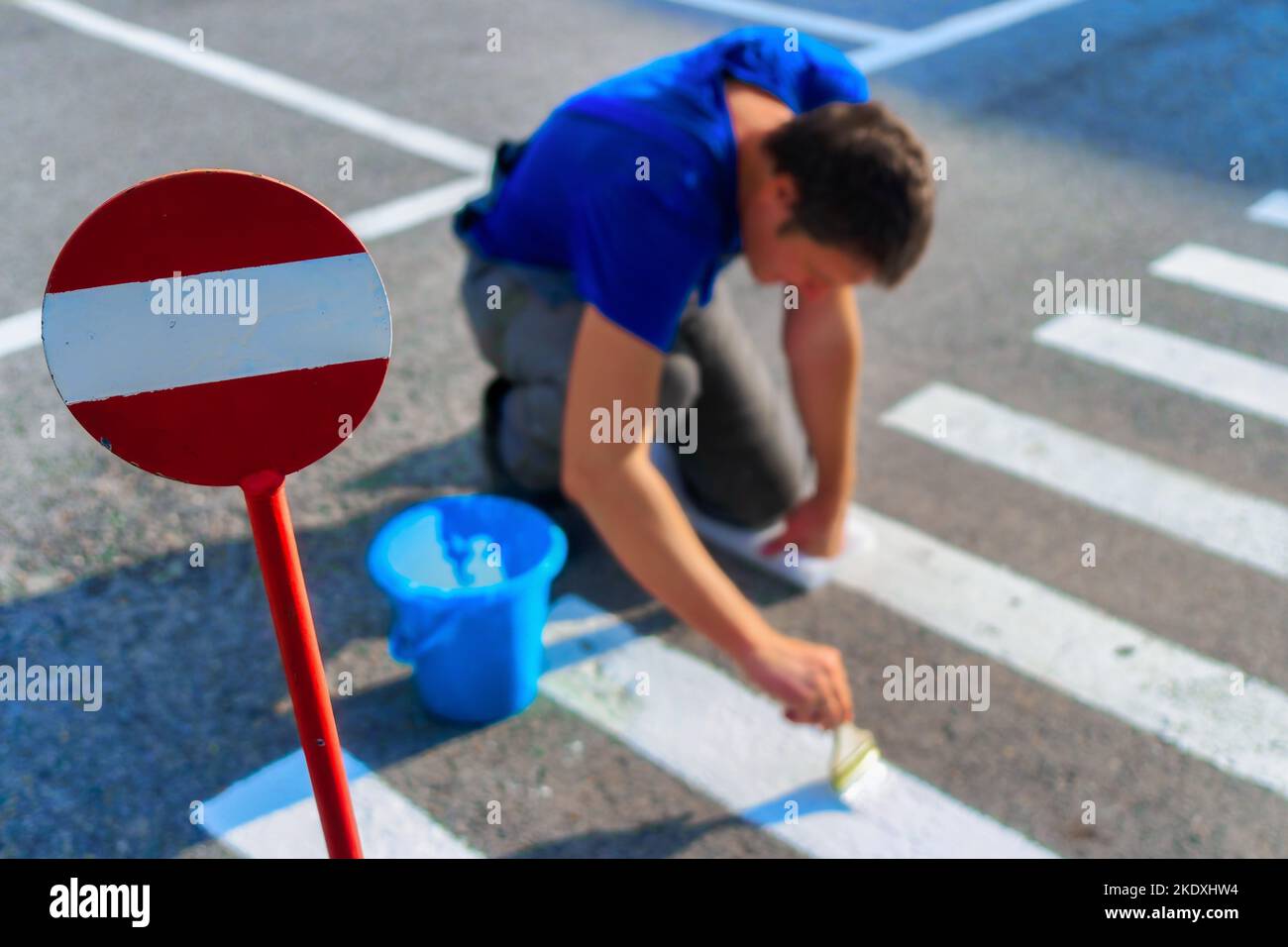 Road service worker paints striped pedestrian crossing on asphalt with ...