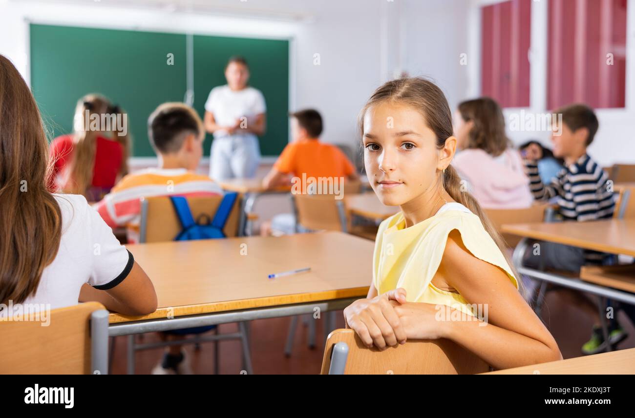 Schoolgirl sits half-turned at desk in classroom at lesson in ...