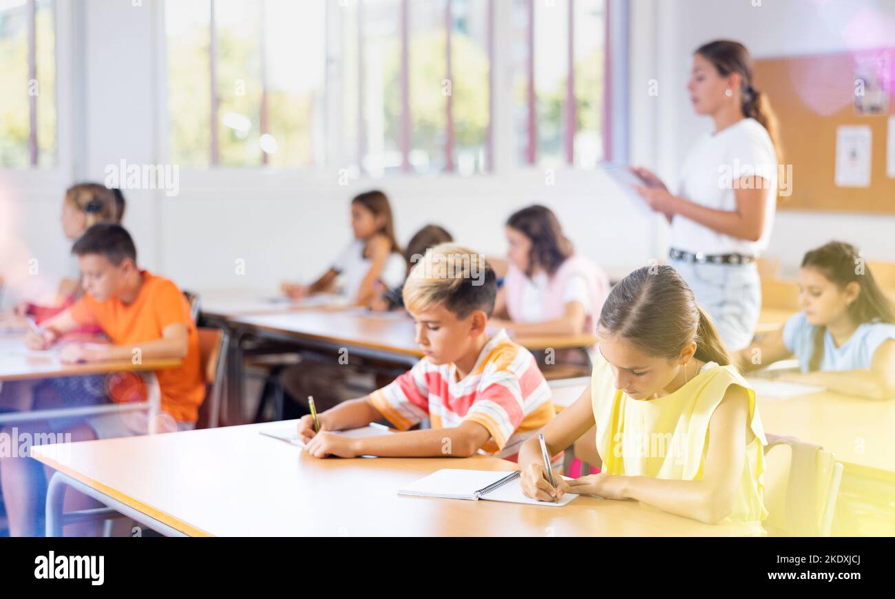 School kids with pens and notebooks studying in classroom with teacher ...