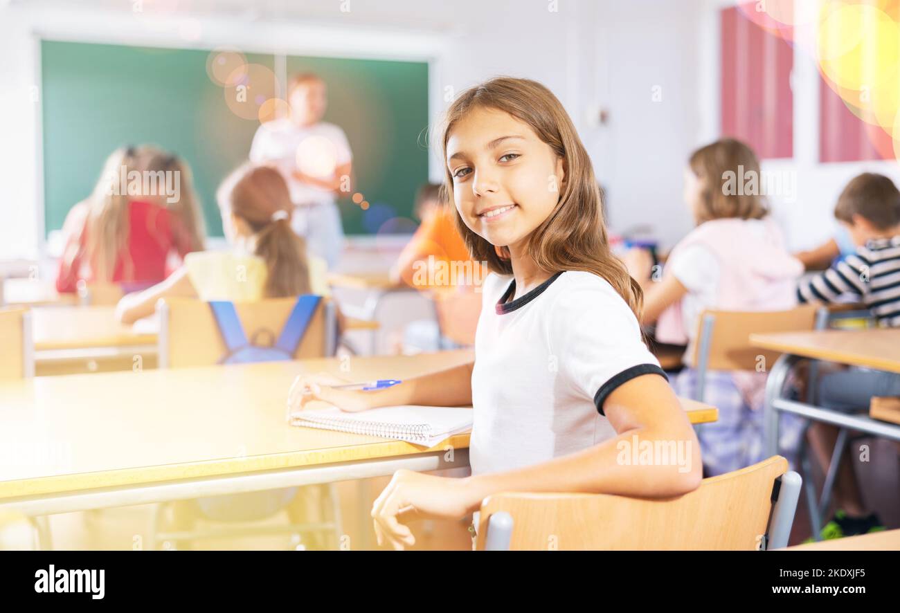 Schoolgirl sits half-turned at desk in classroom at lesson in ...