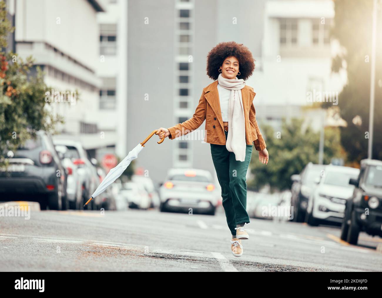 Black woman, umbrella and jump on street, city or road outdoors. Happy ...