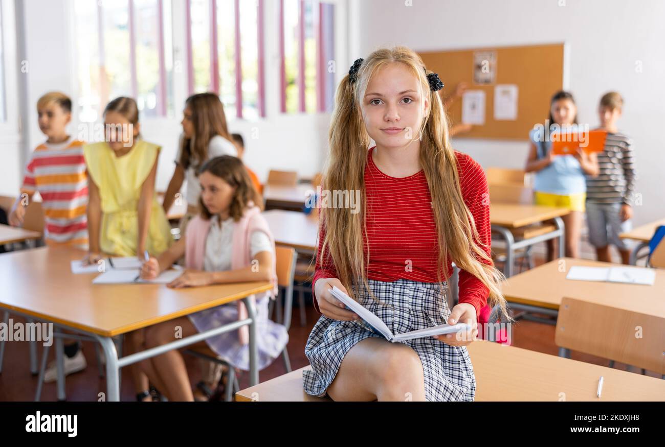 Happy tween schoolgirl sitting on table with notebook during break ...