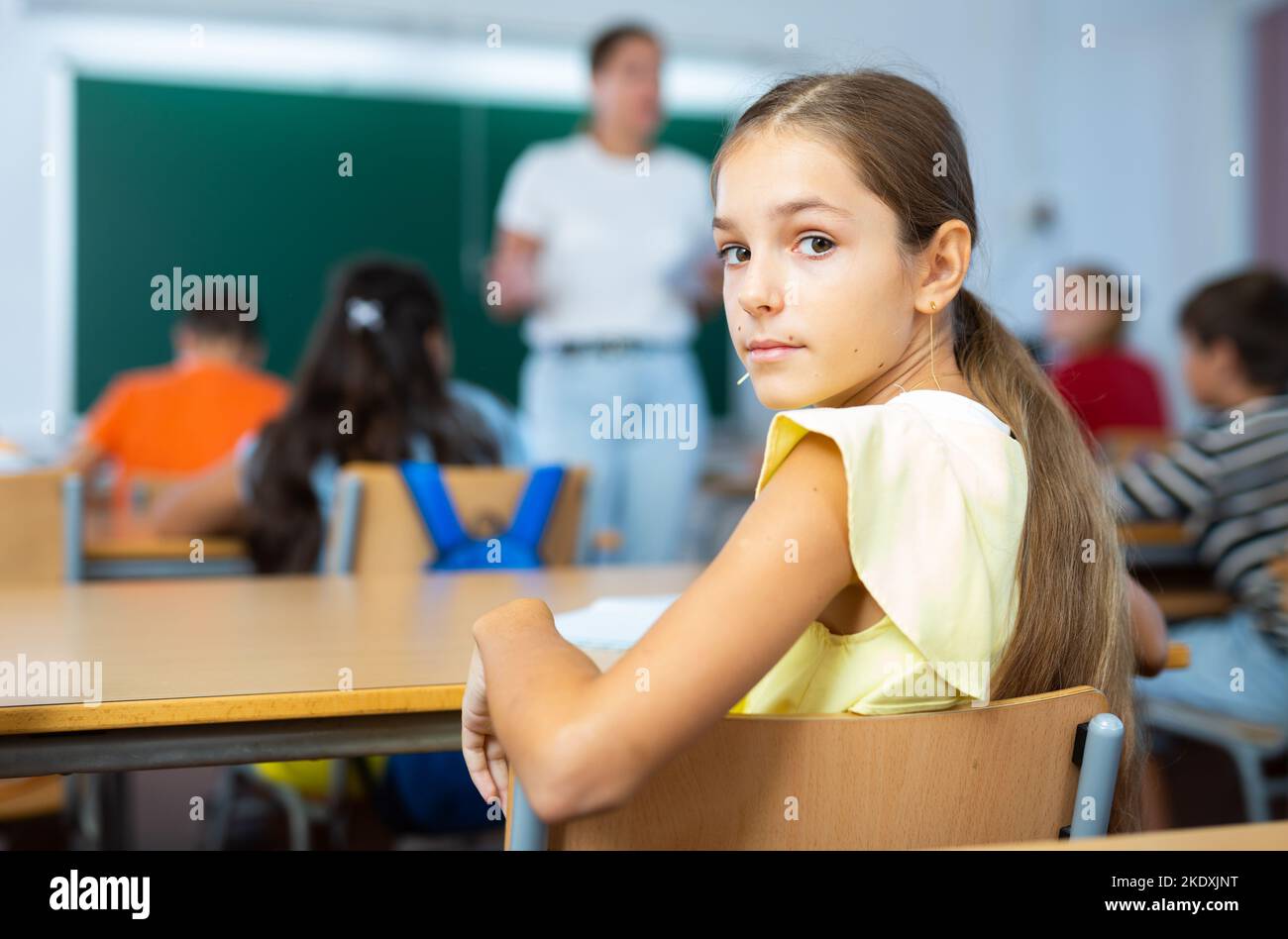 Schoolgirl sits half-turned at desk in classroom at lesson in ...